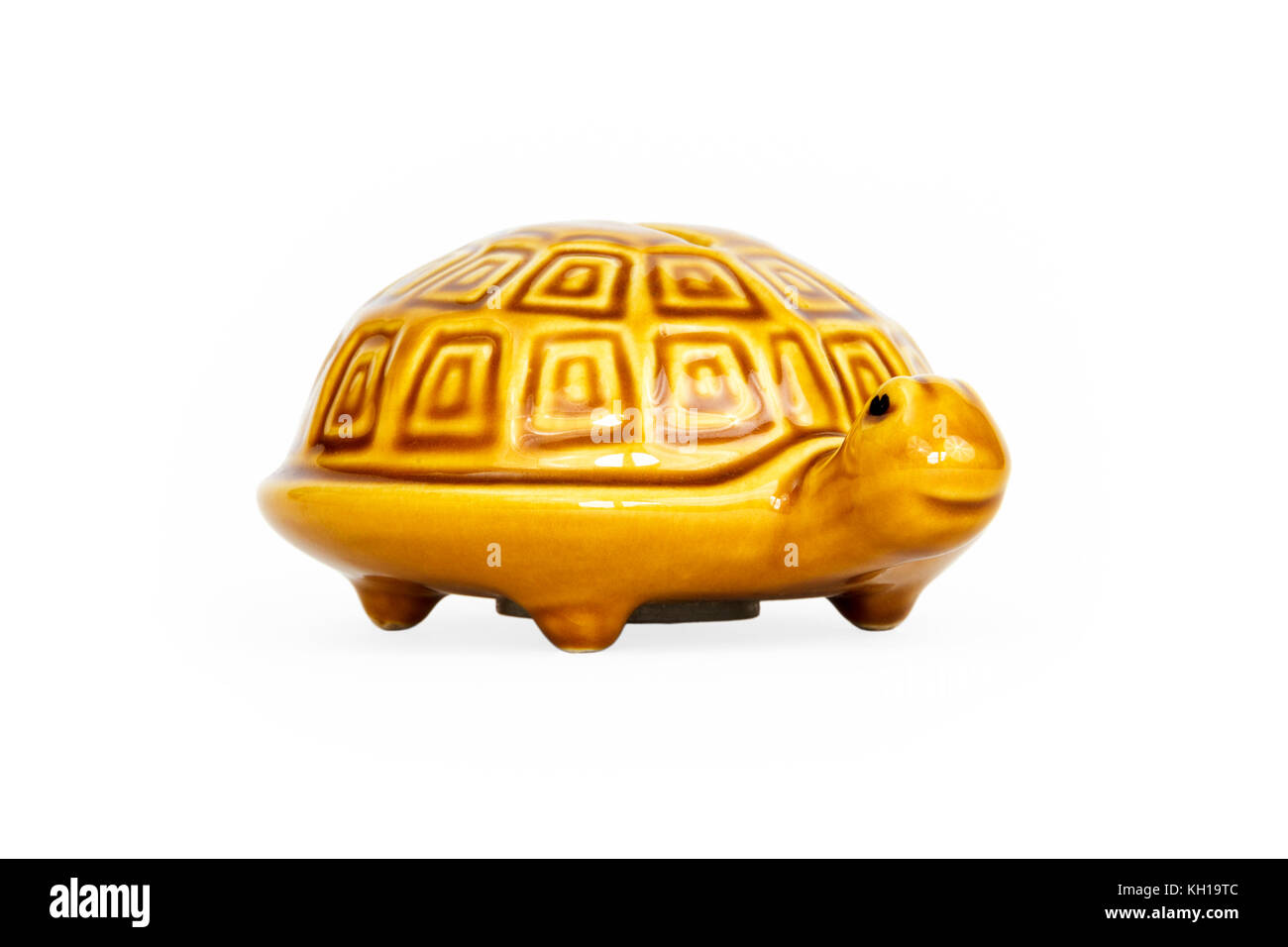 A glazed yellow or orange ceramic tortoise money box, against a white ...