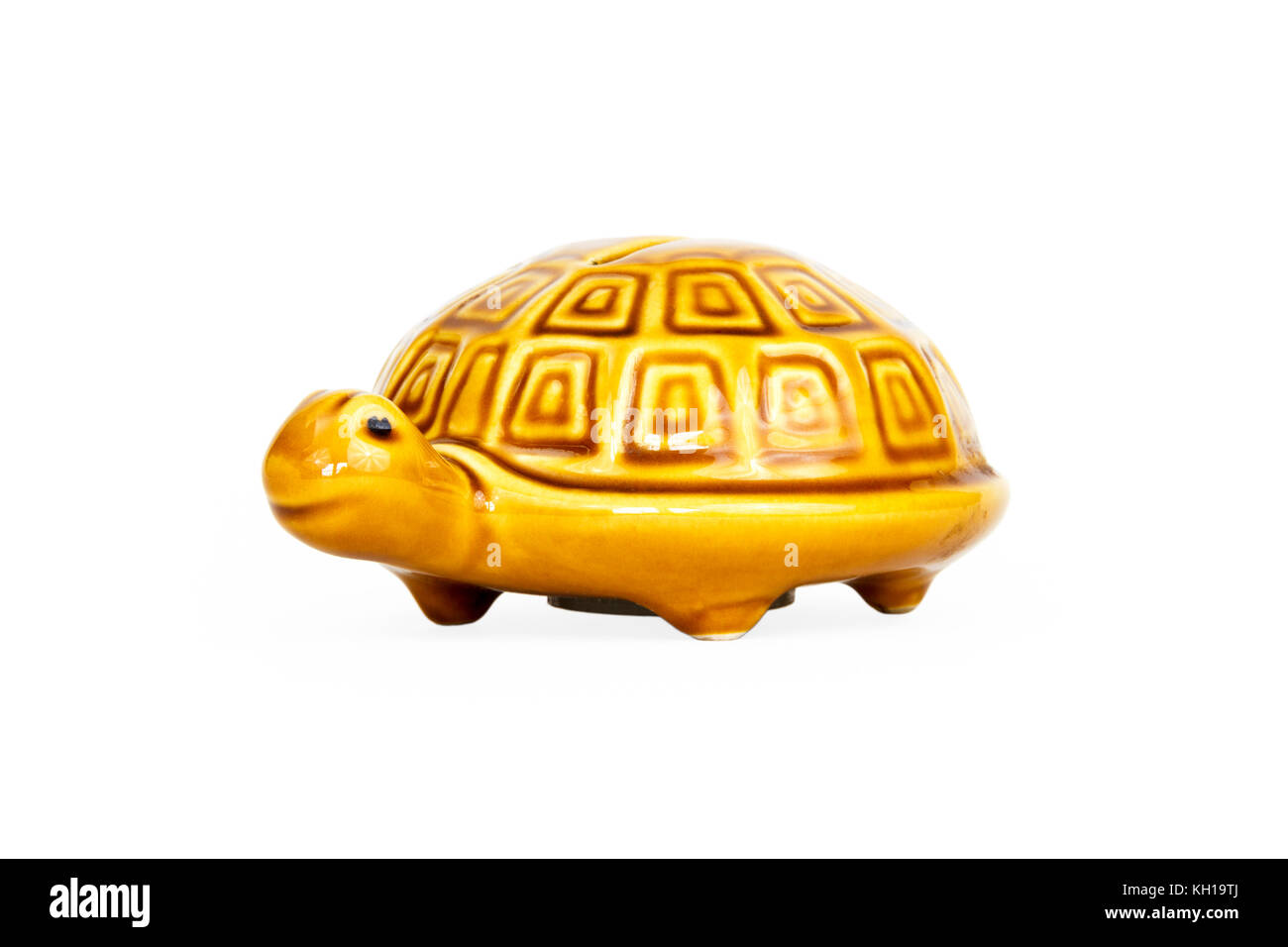 A glazed yellow or orange ceramic tortoise money box, against a white ...