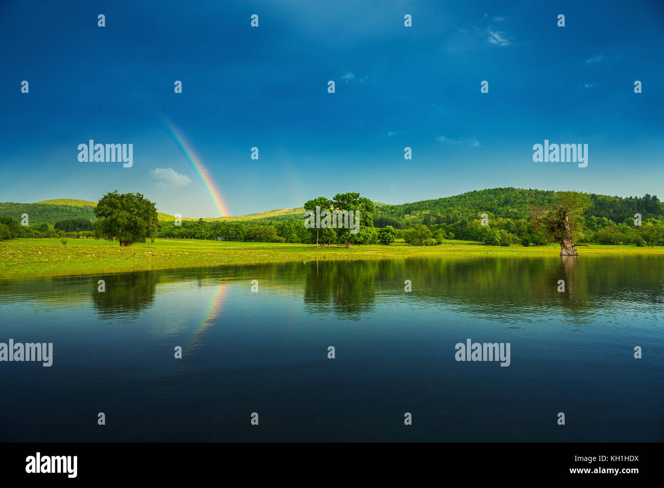 Rainbow over a lake, reflected in the water Stock Photo - Alamy