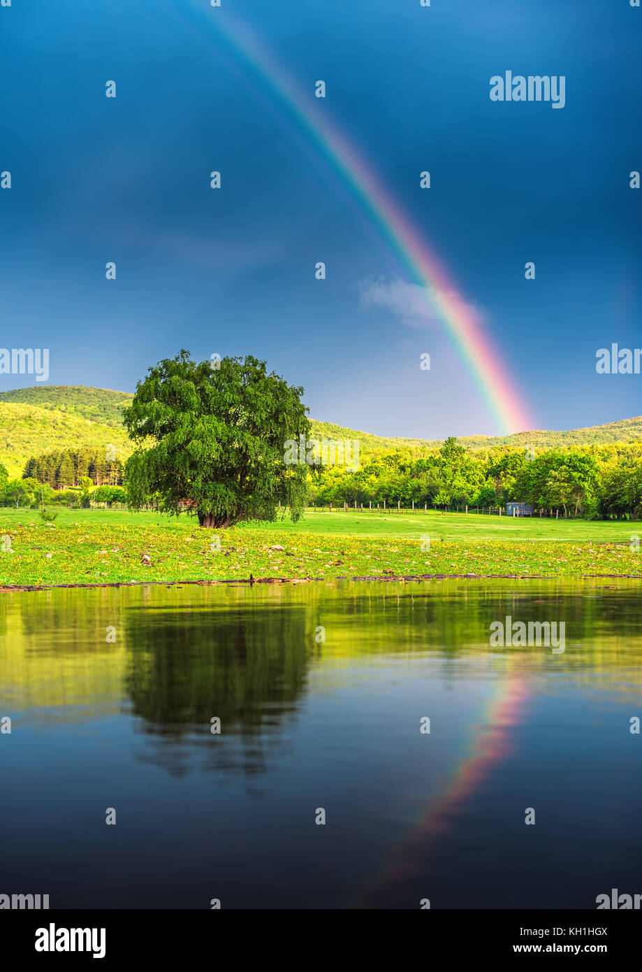 Rainbow over a lake, reflected in the water Stock Photo - Alamy