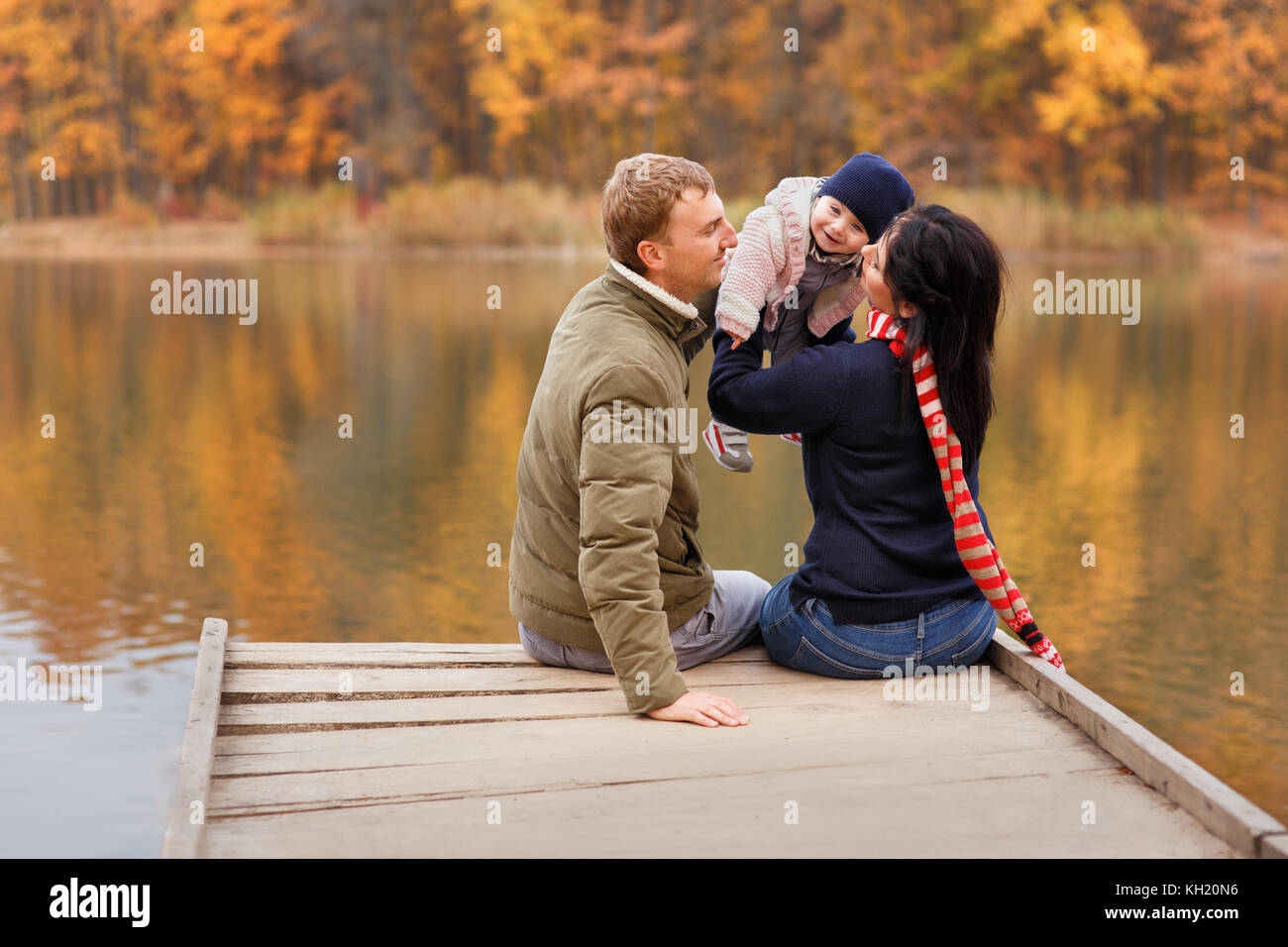 young parents sitting on wooden bridge and play with little daughter ...