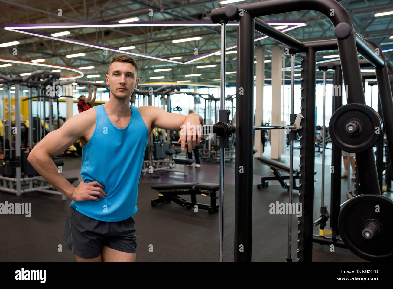 Portrait of muscular fitness trainer standing leaning on machines in ...