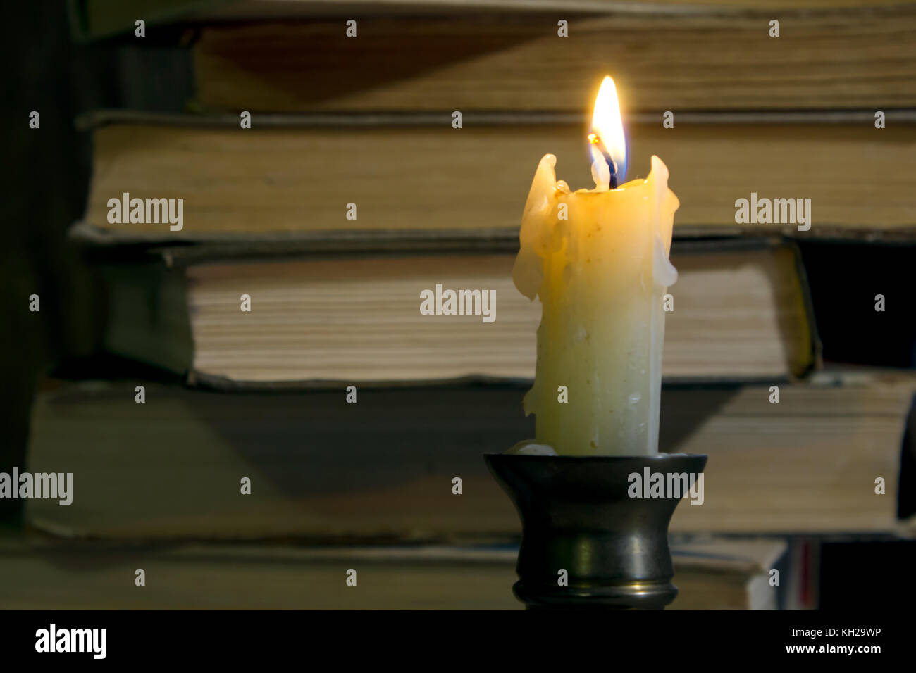 Burning candle against the background of a stack of old books Stock ...