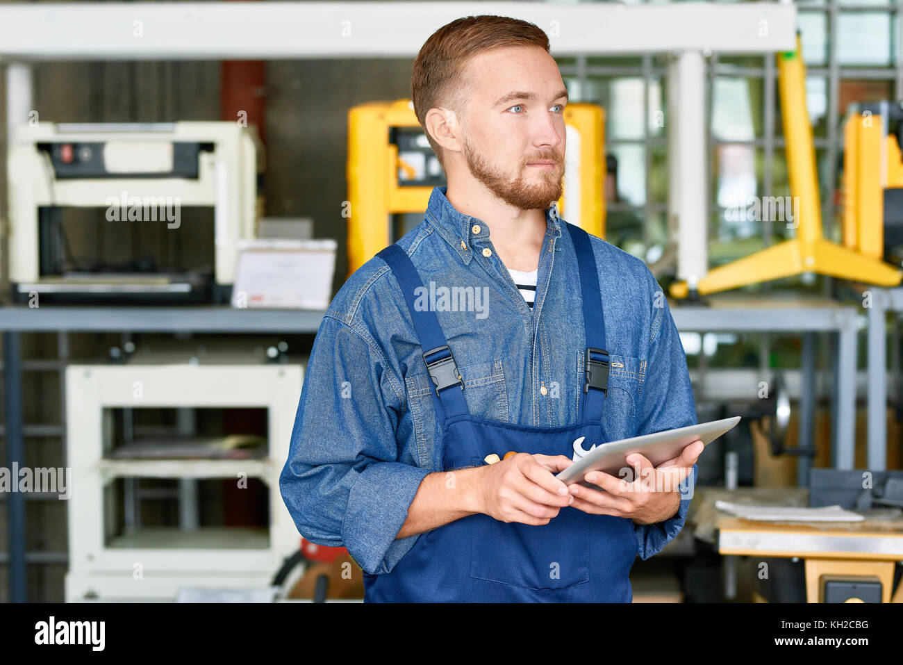 Portrait of young man working at modern factory operating machine units ...