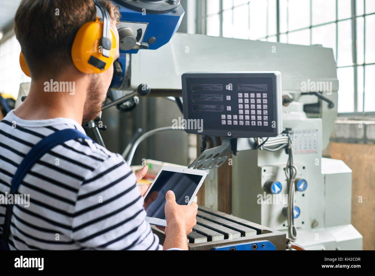 Back view portrait of young factory worker operating machine units at ...