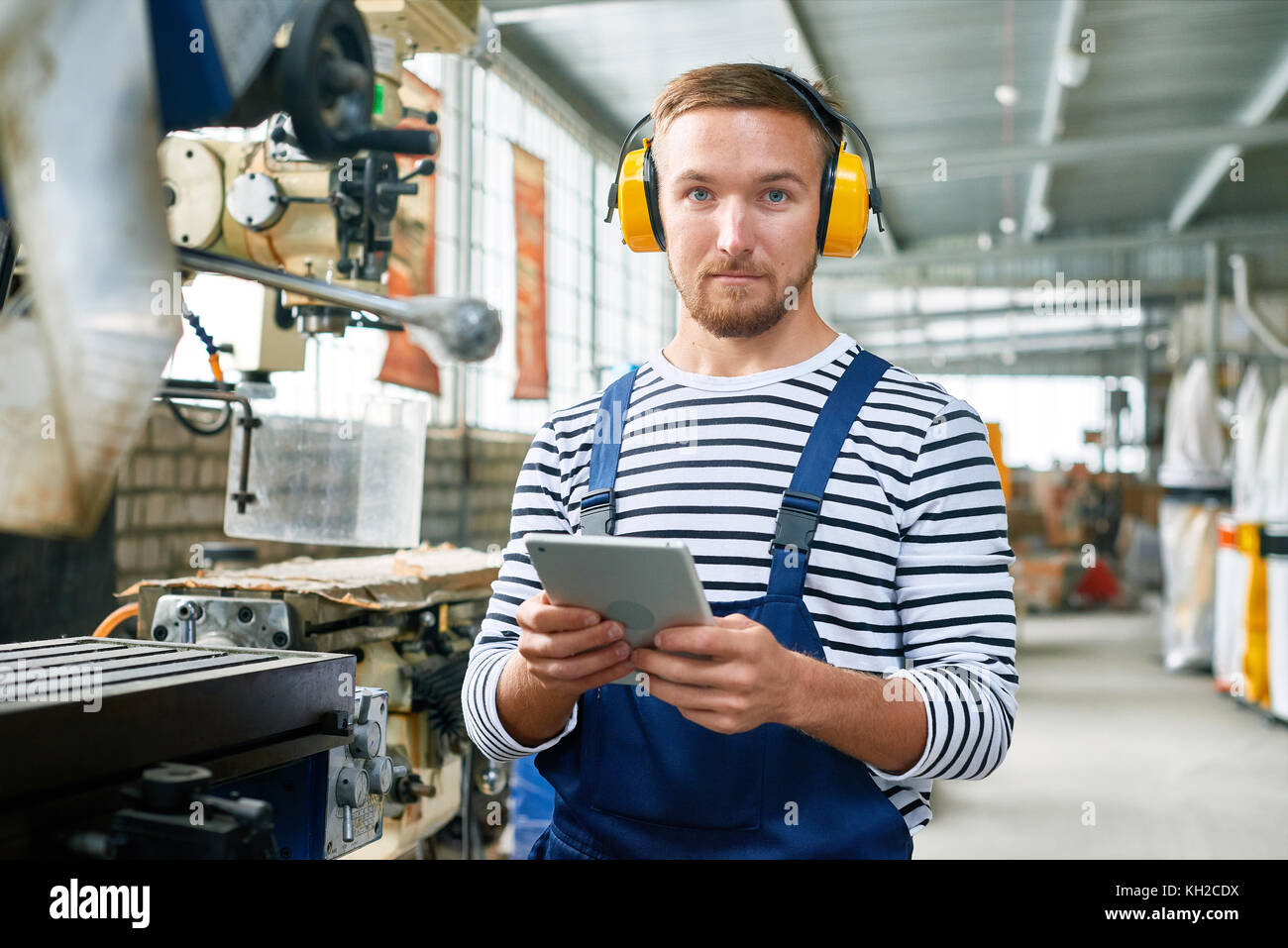 Portrait of factory worker operating machine units at modern factory using digital tablet with ...