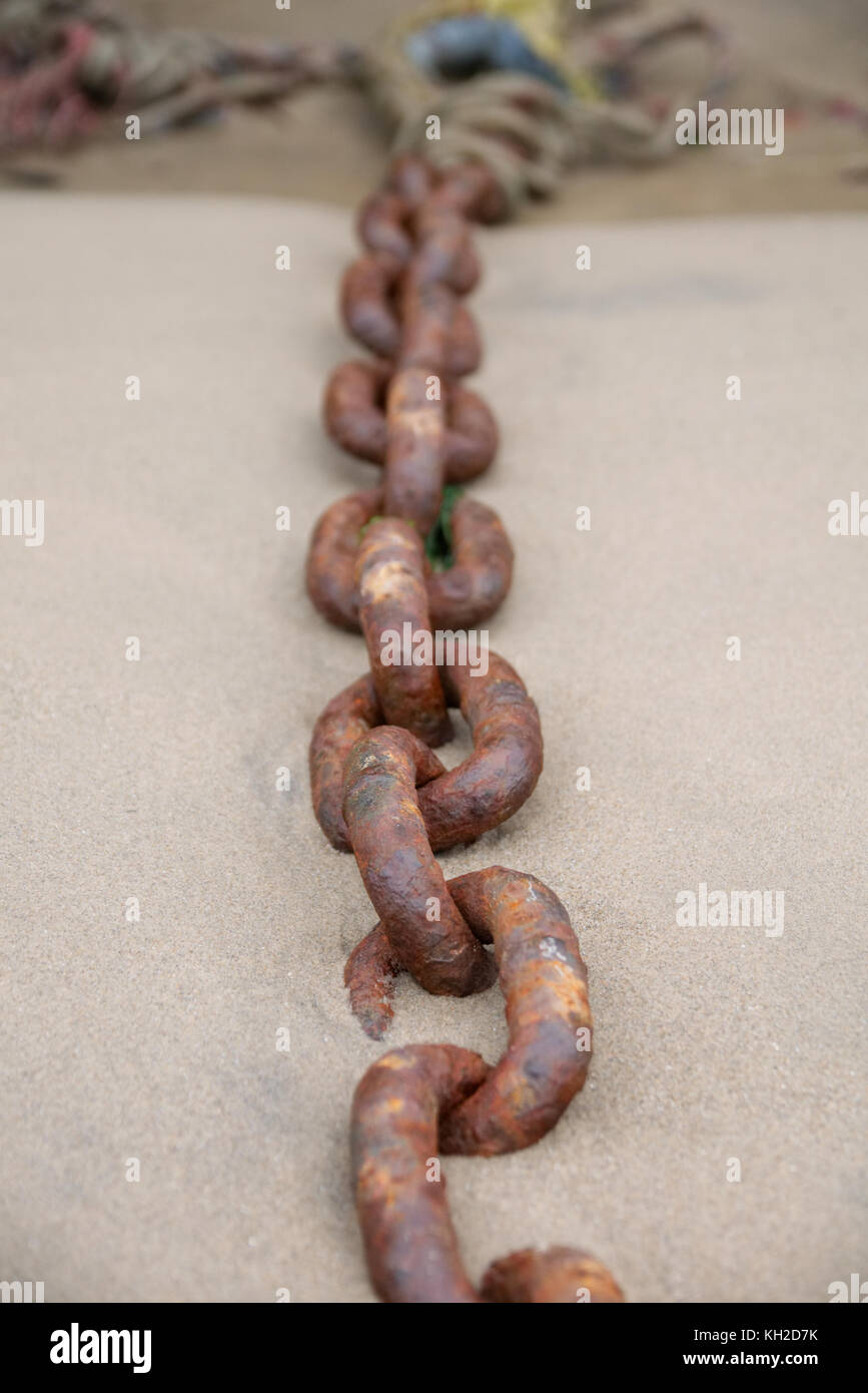 Rusty old boat chain on a sandy beach with a shallow depth of field ...