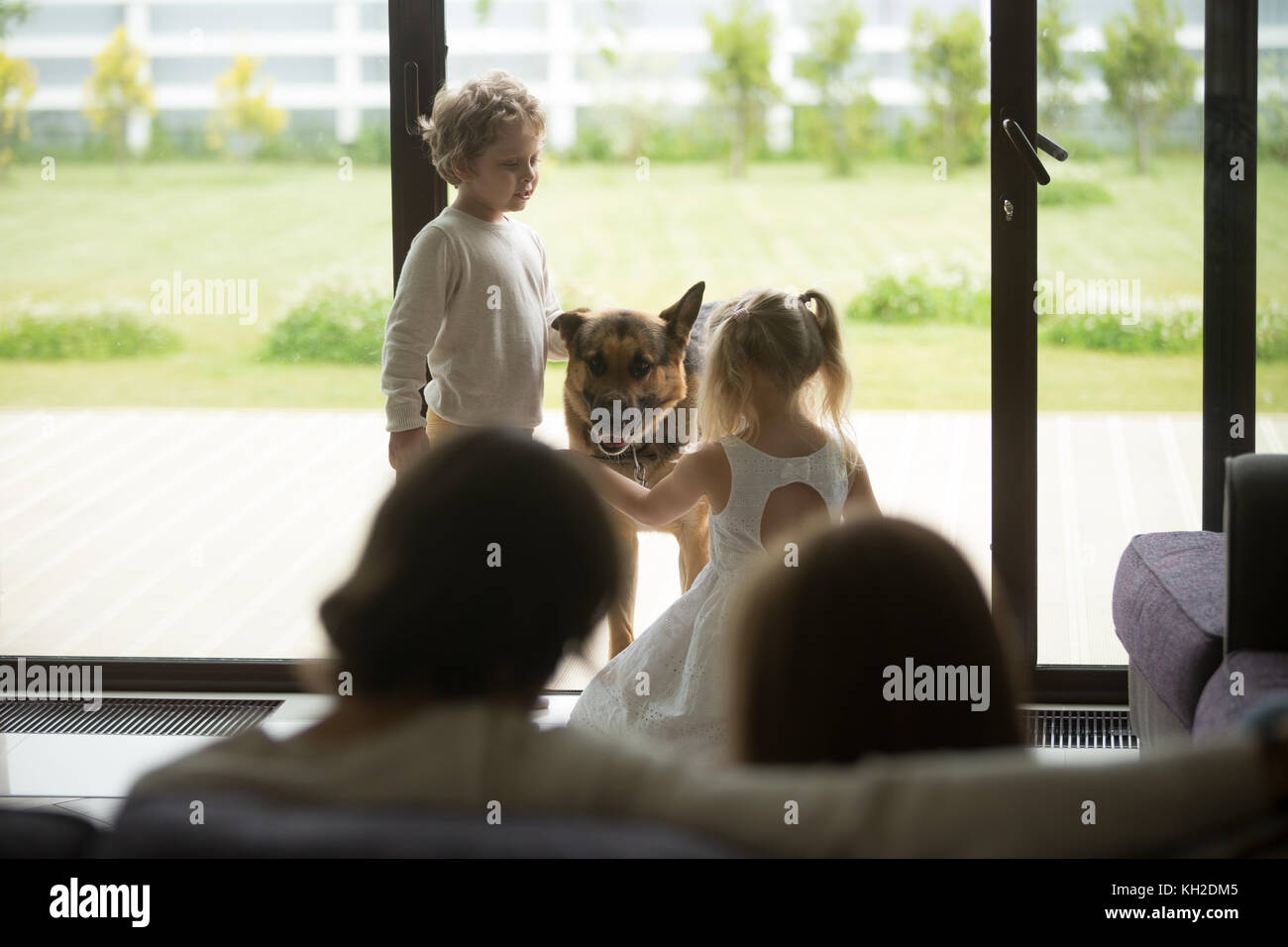 Little boy and girl playing with dog coming into house from yard, rear ...