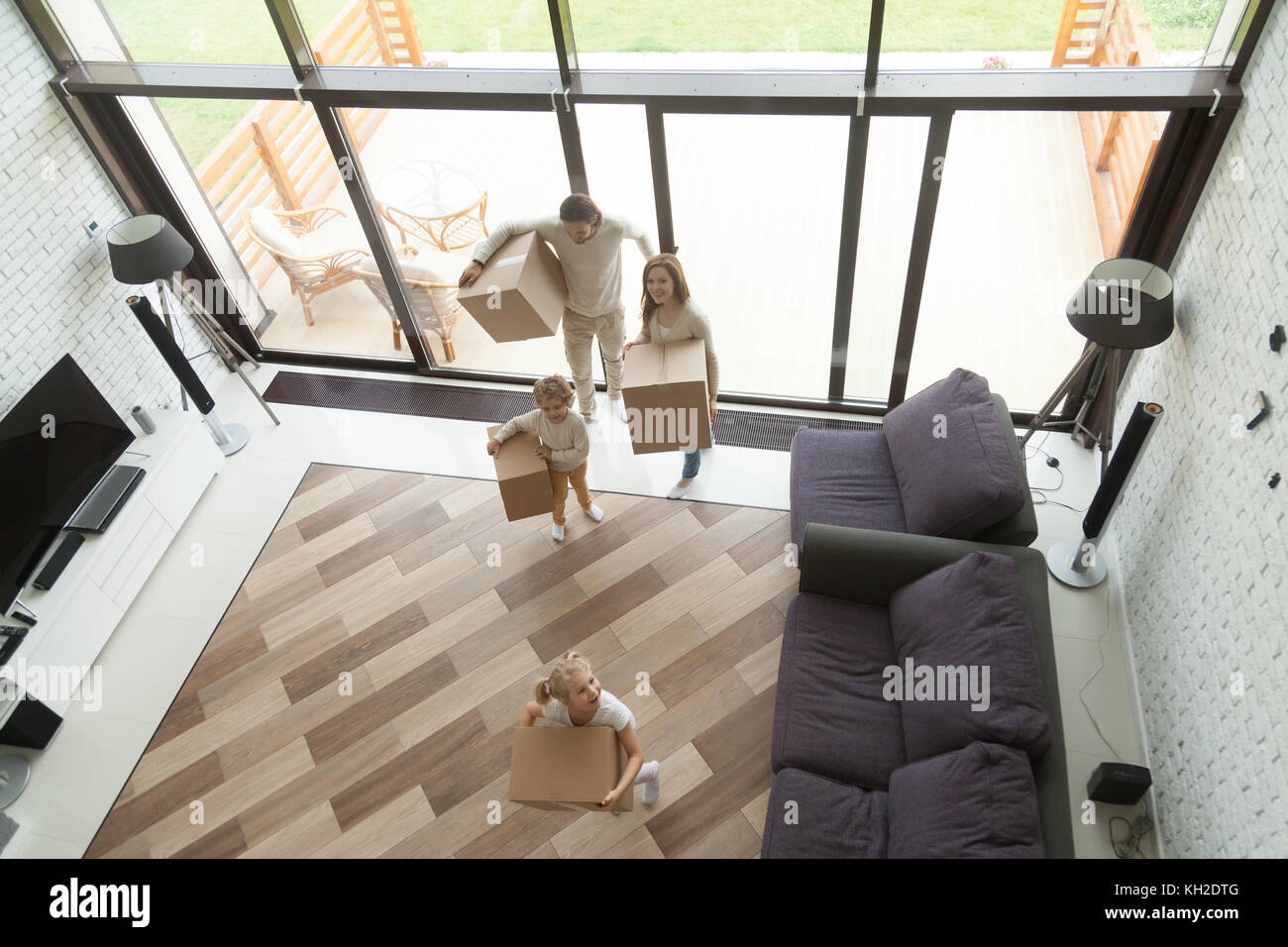 Happy family with kids carrying boxes entering into big modern house ...