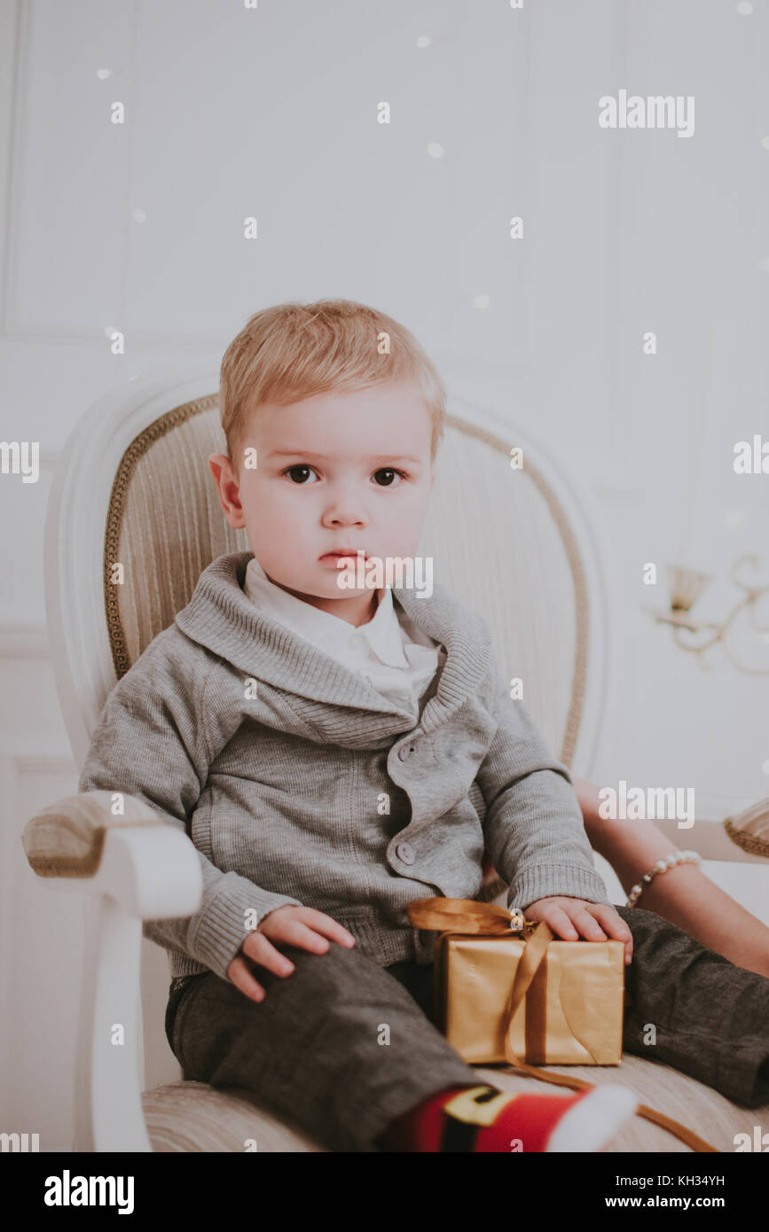 Cheerful little baby boy playing near Christmas tree, gold and beige ...