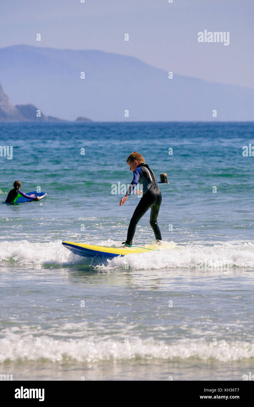 Boy learning to stand on a surfing board and surfs on a small wave on a ...