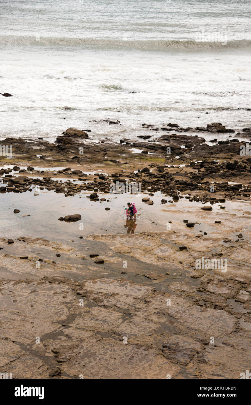Father and two young daughters explore a wave-cut rock bench at ...