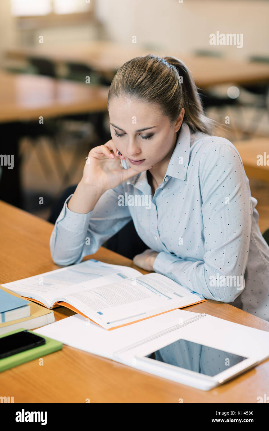 Efficient female student at the library, she is sitting at desk and ...