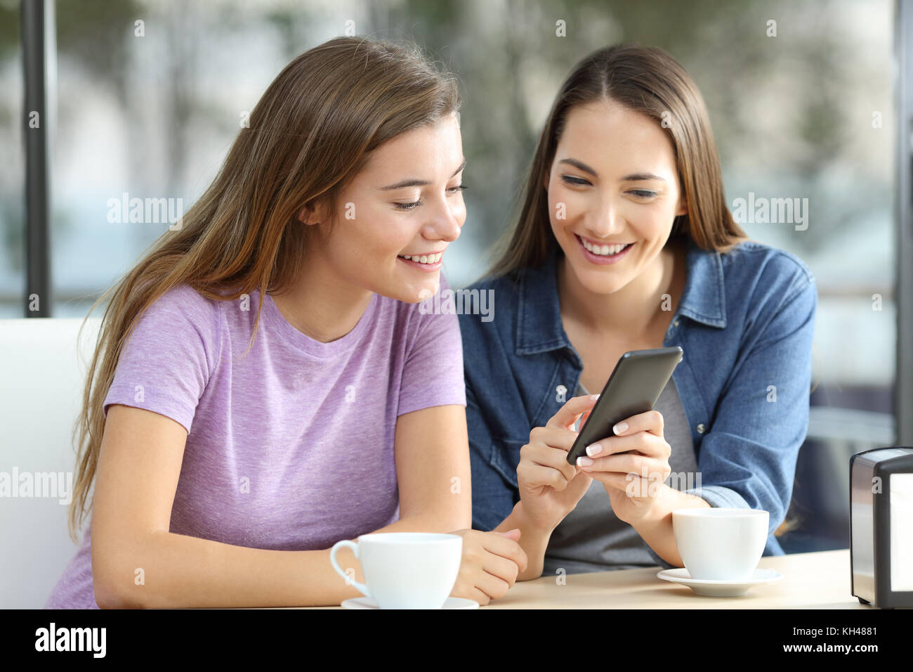 Two happy friends sharing on line content with a smart phone in a ...