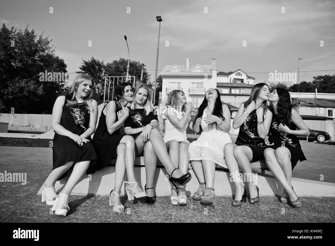 Group of 7 girls wear on black and 2 brides sitting on bench and having ...