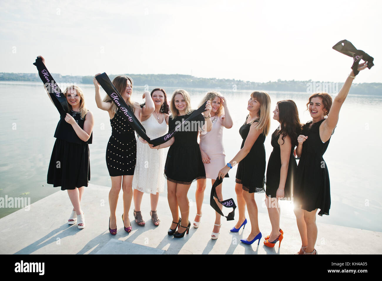 Group of 8 girls wear on black and 2 brides at hen party against sunny ...