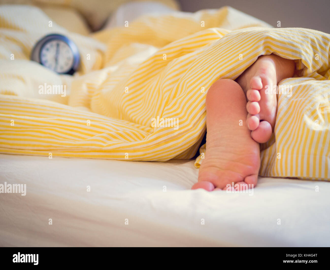 Feet sticking out from under covers and alarm clock in the background ...