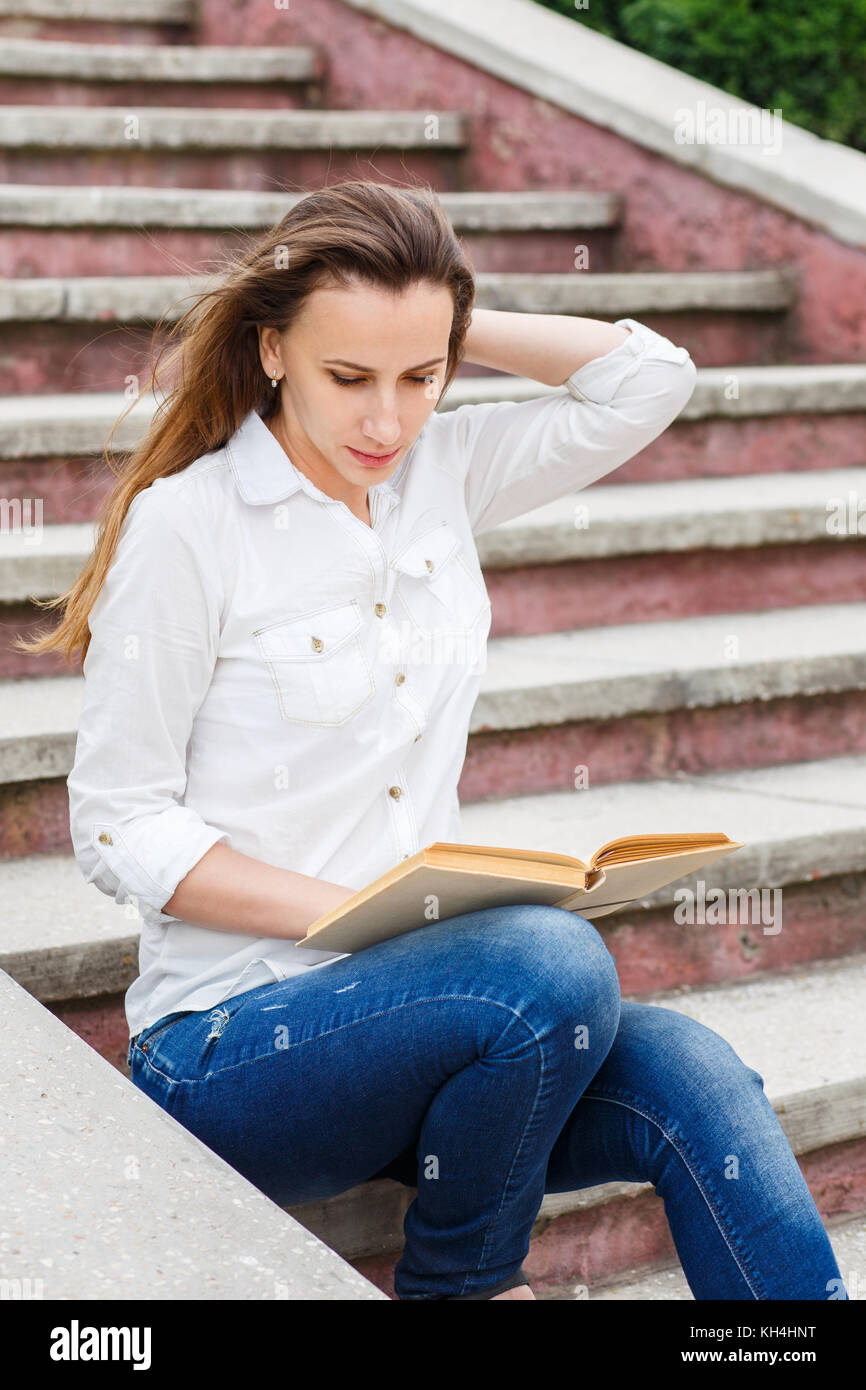 Young woman sitting on stairs and reading a book. Beautiful european ...