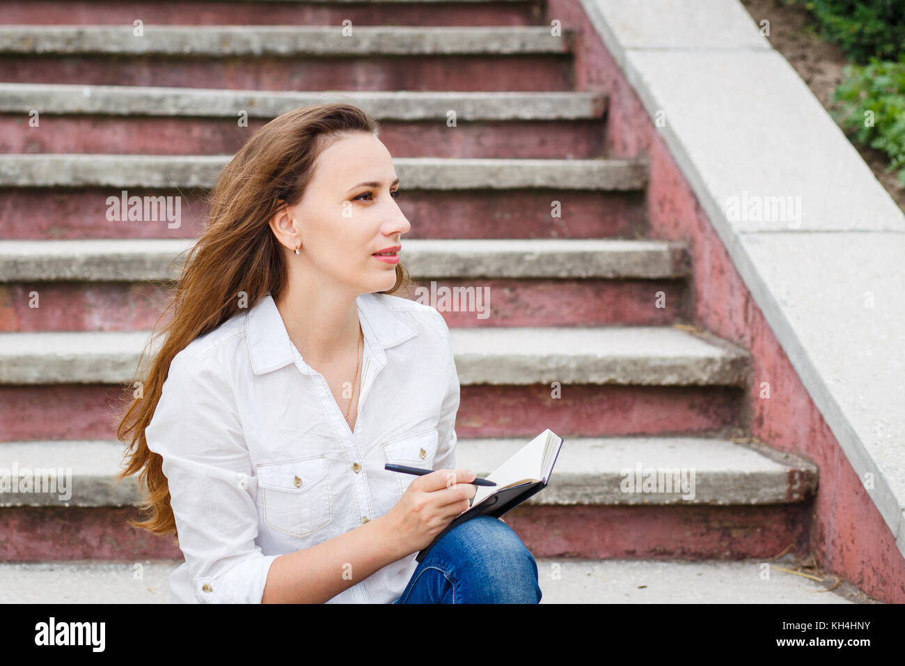 Young woman sitting on stairs and making notes in notebook Stock Photo ...