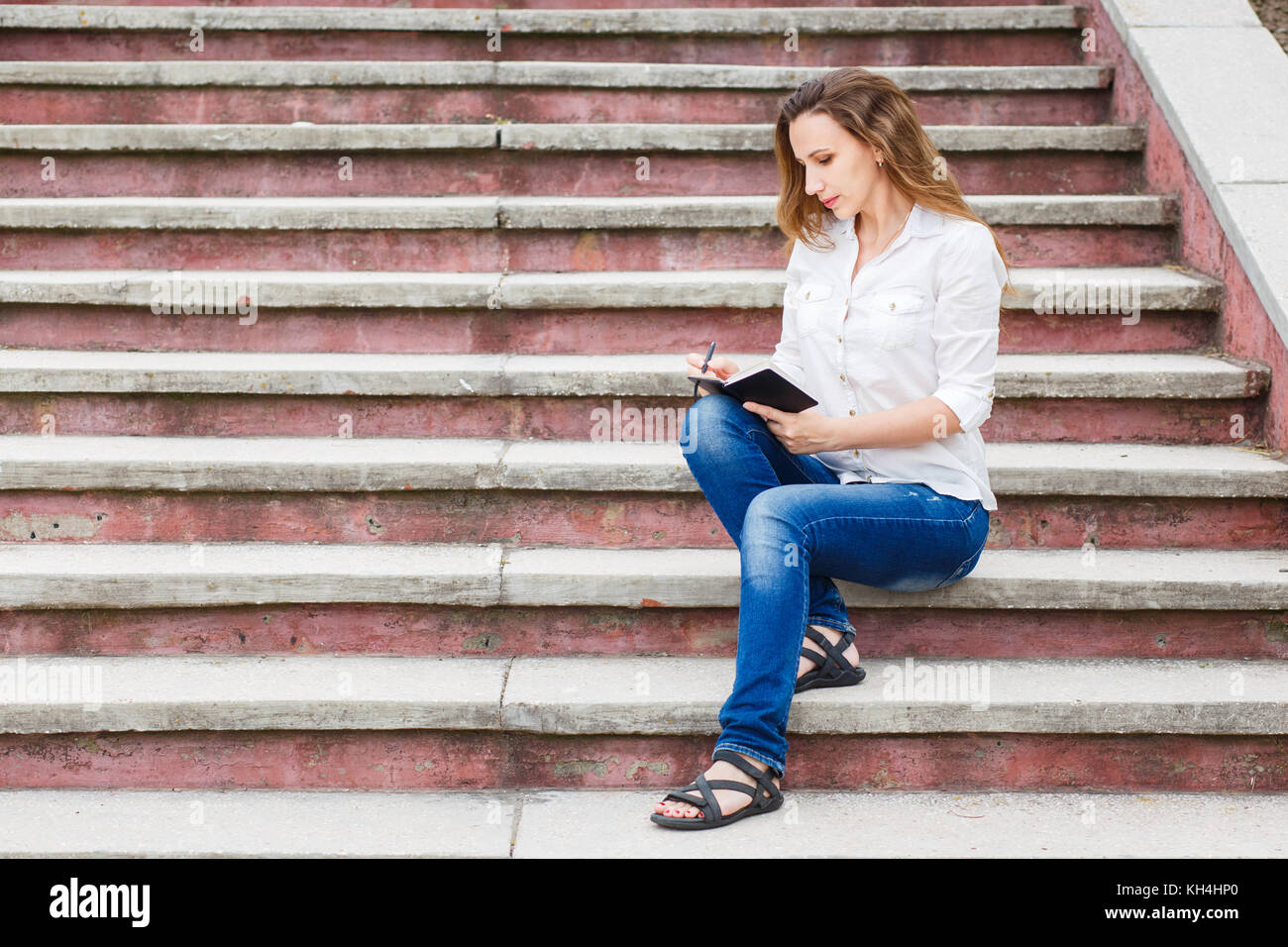 Young woman sitting on stairs and making notes in notebook Stock Photo ...