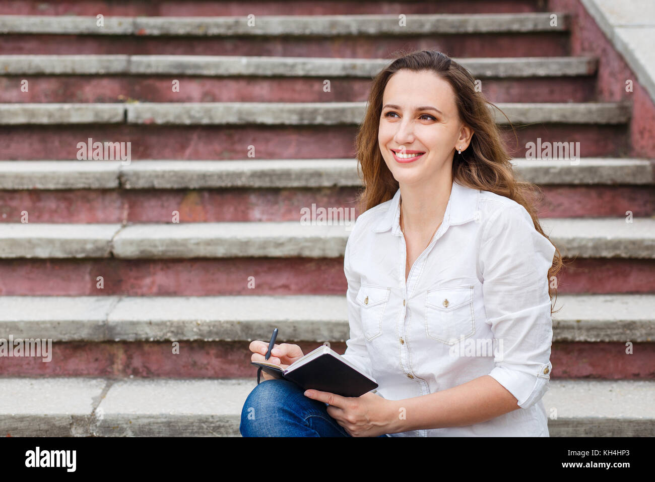 Young woman sitting on stairs and making notes in notebook Stock Photo ...