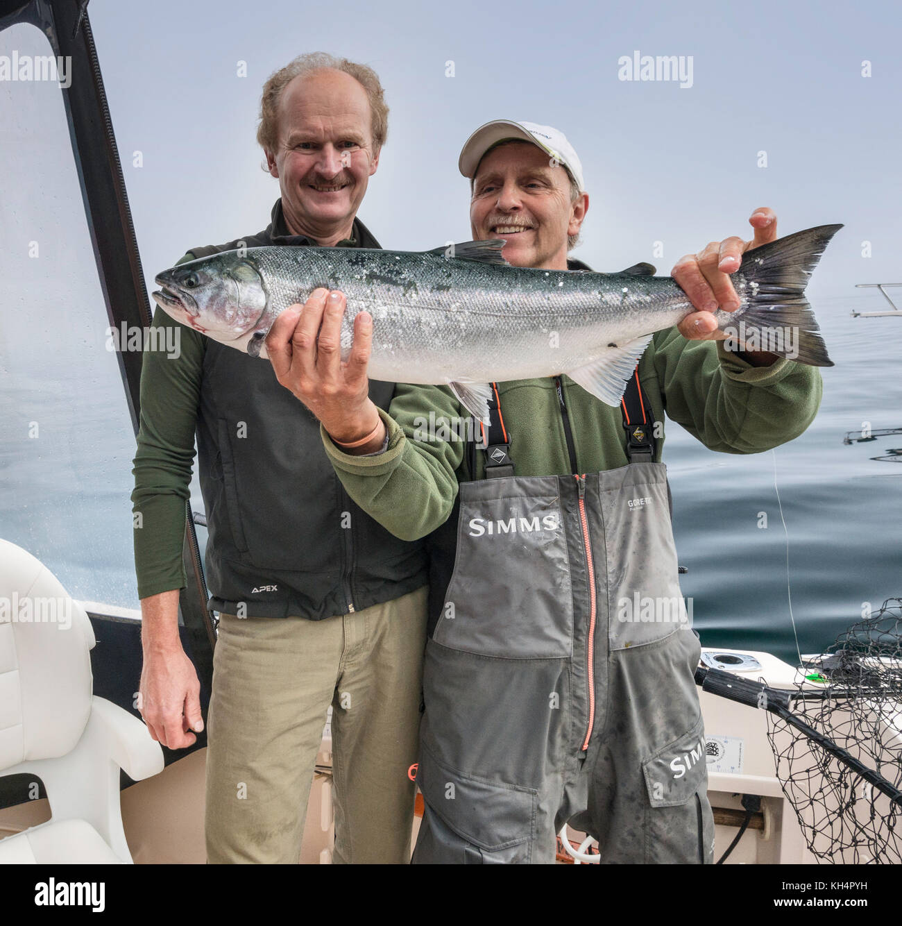 Two middle-aged men on fishing boat, with a caught salmon, foggy ...
