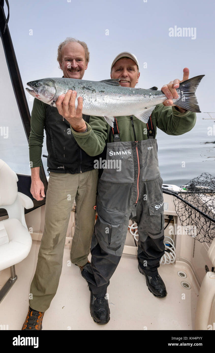 Two middle-aged men on fishing boat, with a caught salmon, foggy ...