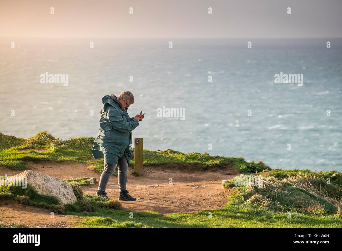A woman using her smartphone in windy conditions standing on a footpath ...