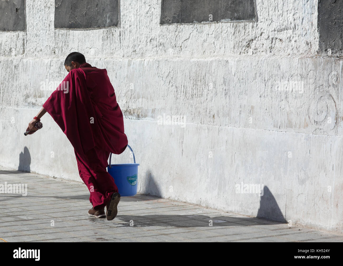 Tibetan monk carrying bucket for the painting of a temple in Rongwo ...