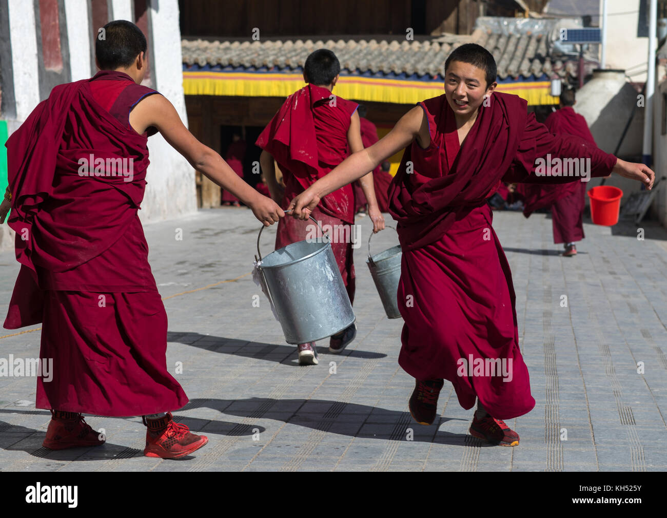 Monks carrying buckets for the painting of a temple in Rongwo monastery ...