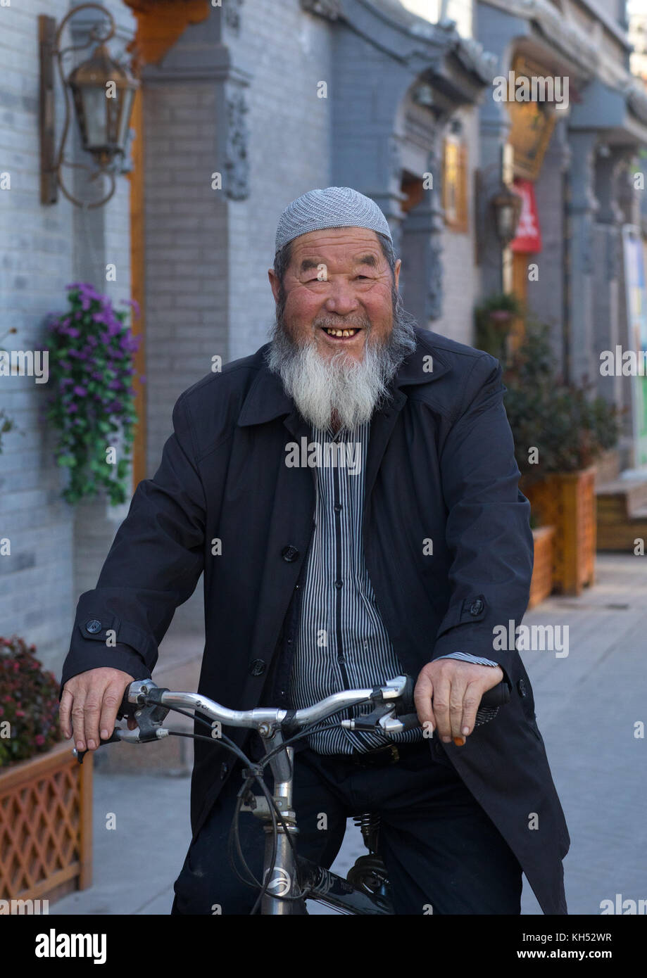 Smiling hui muslim man riding a bicycle in the street , Gansu province ...