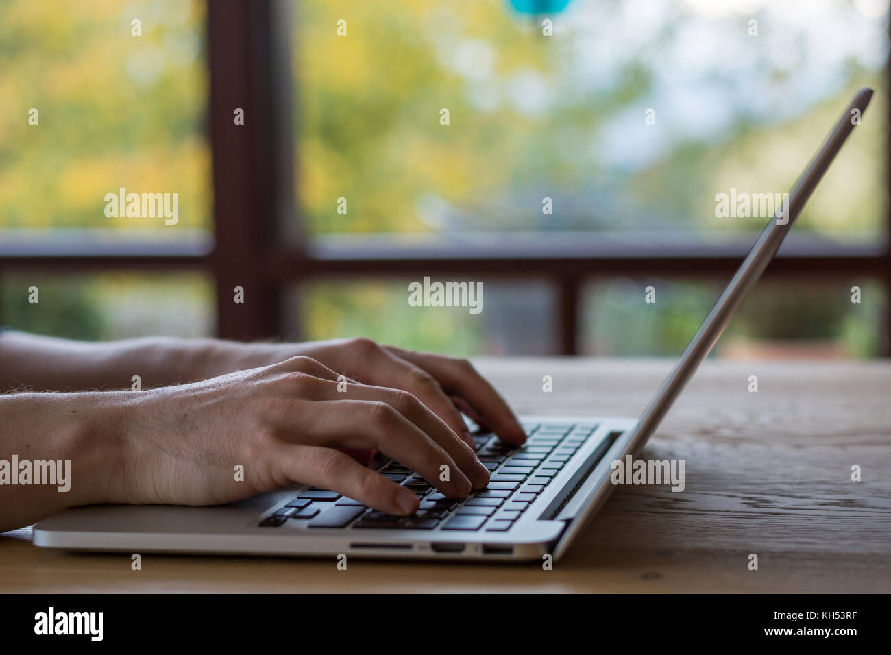 Typing on a laptop in front of window on wooden table Stock Photo - Alamy