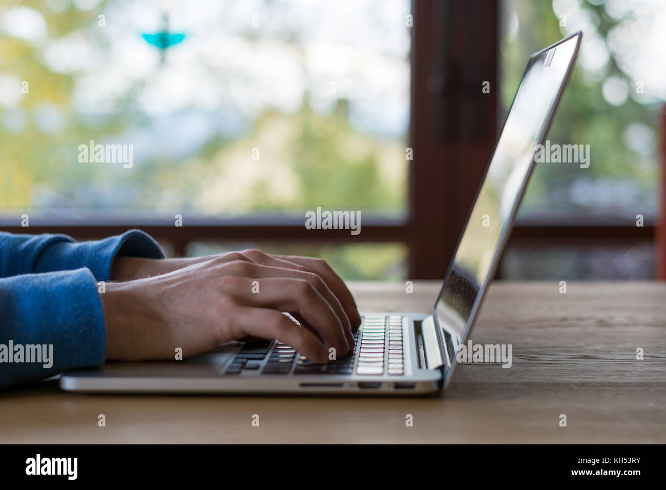 Typing on a laptop in front of window on wooden table Stock Photo - Alamy