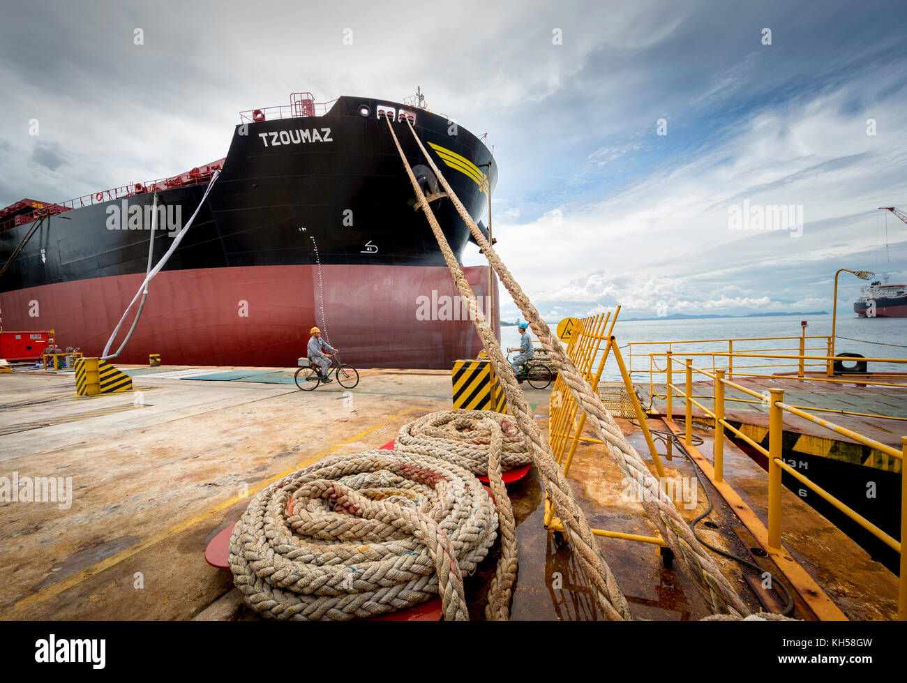 Worker is riding a bicycle in front of the ship docked in dockyard ...