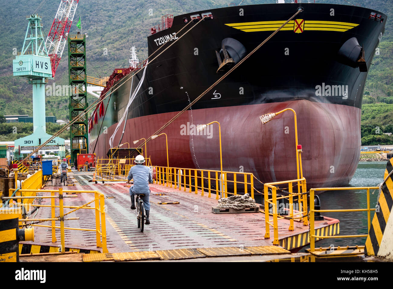 Worker is riding a bicycle in front of the ship docked in dockyard ...