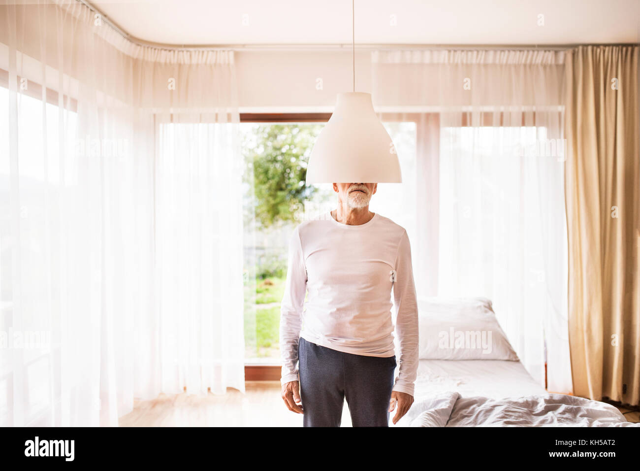 Senior man standing behind pendant lamp at home Stock Photo - Alamy