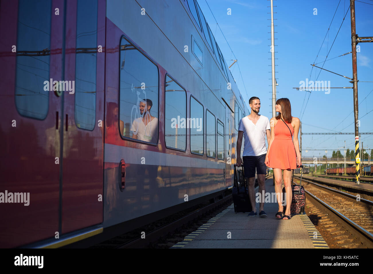 Happy young caucasian couple walking next to the train, pulling ...