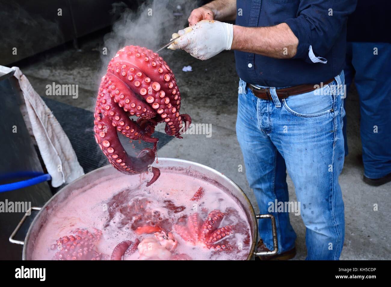 Unrecognizable man holding red octopus above pot with boiling water ...
