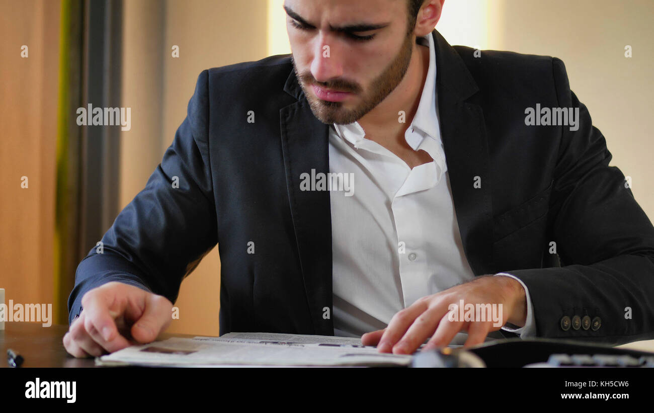 Concentrated man looking through newspaper at work Stock Photo - Alamy