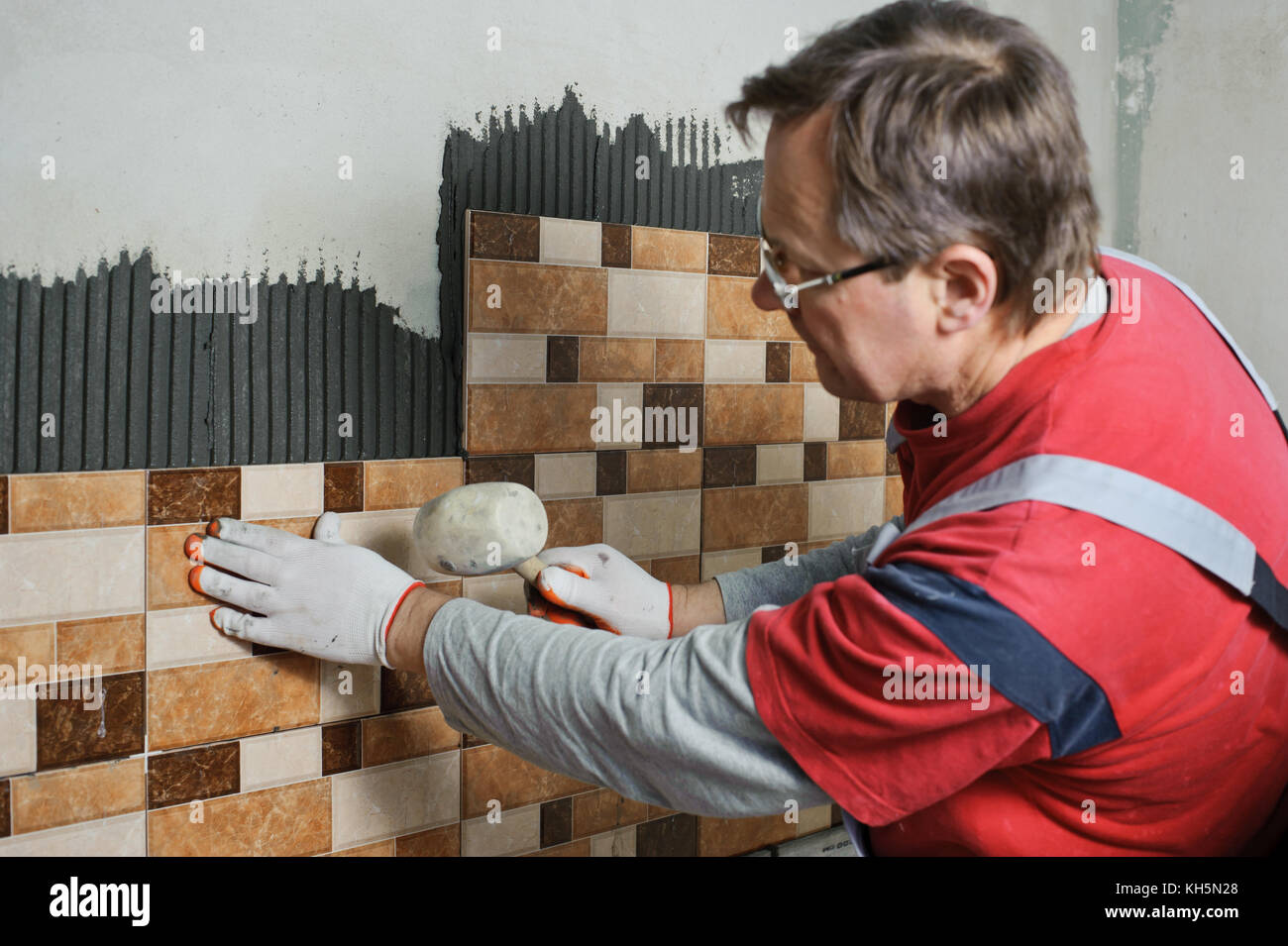 Laying Ceramic Tiles. Tiler knocking on the tiles with a rubber mallet ...