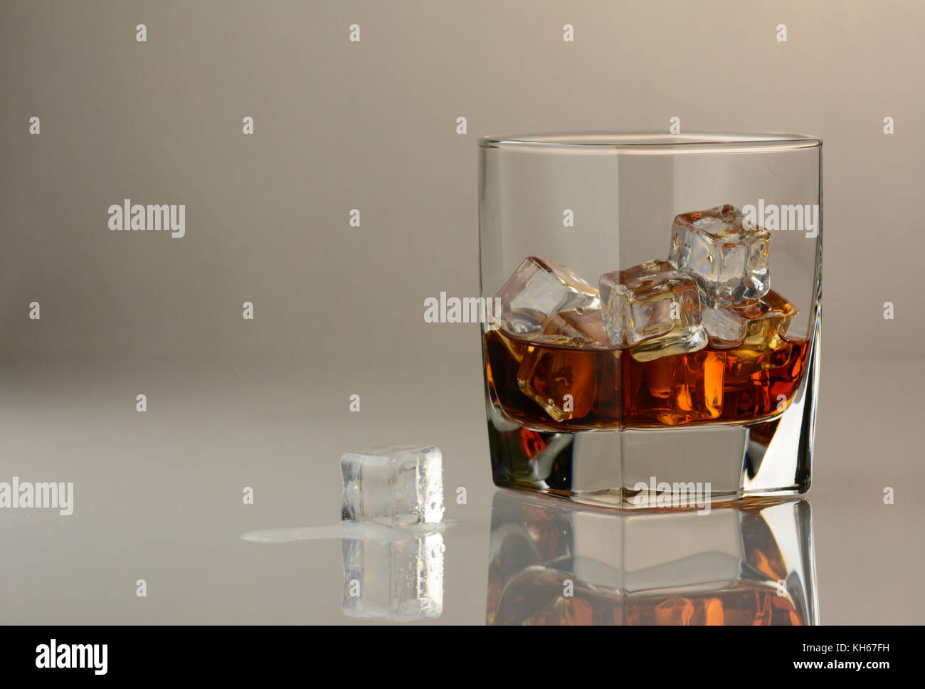 A glass of alcohol on a glass table with a cube of melting ice Stock ...