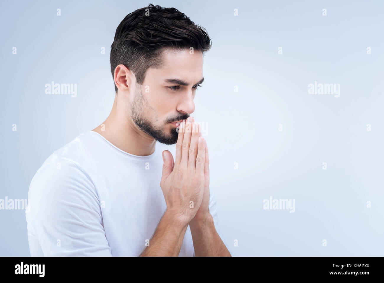 Sad young man praying while standing against the blue background Stock ...