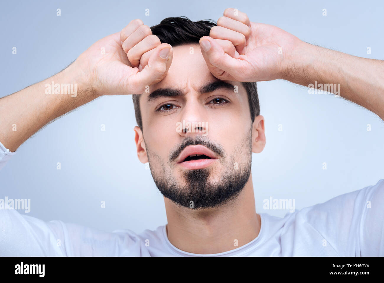Emotional young man pressing his fists to the forehead and looking ...