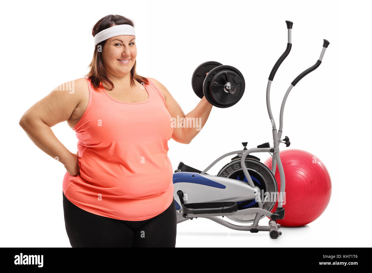 Overweight woman holding a dumbbell in front of a cross trainer machine ...