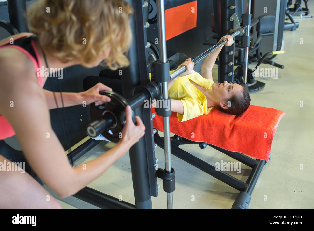 fitness-trainer assisting young female in lifting barbell in the gym ...