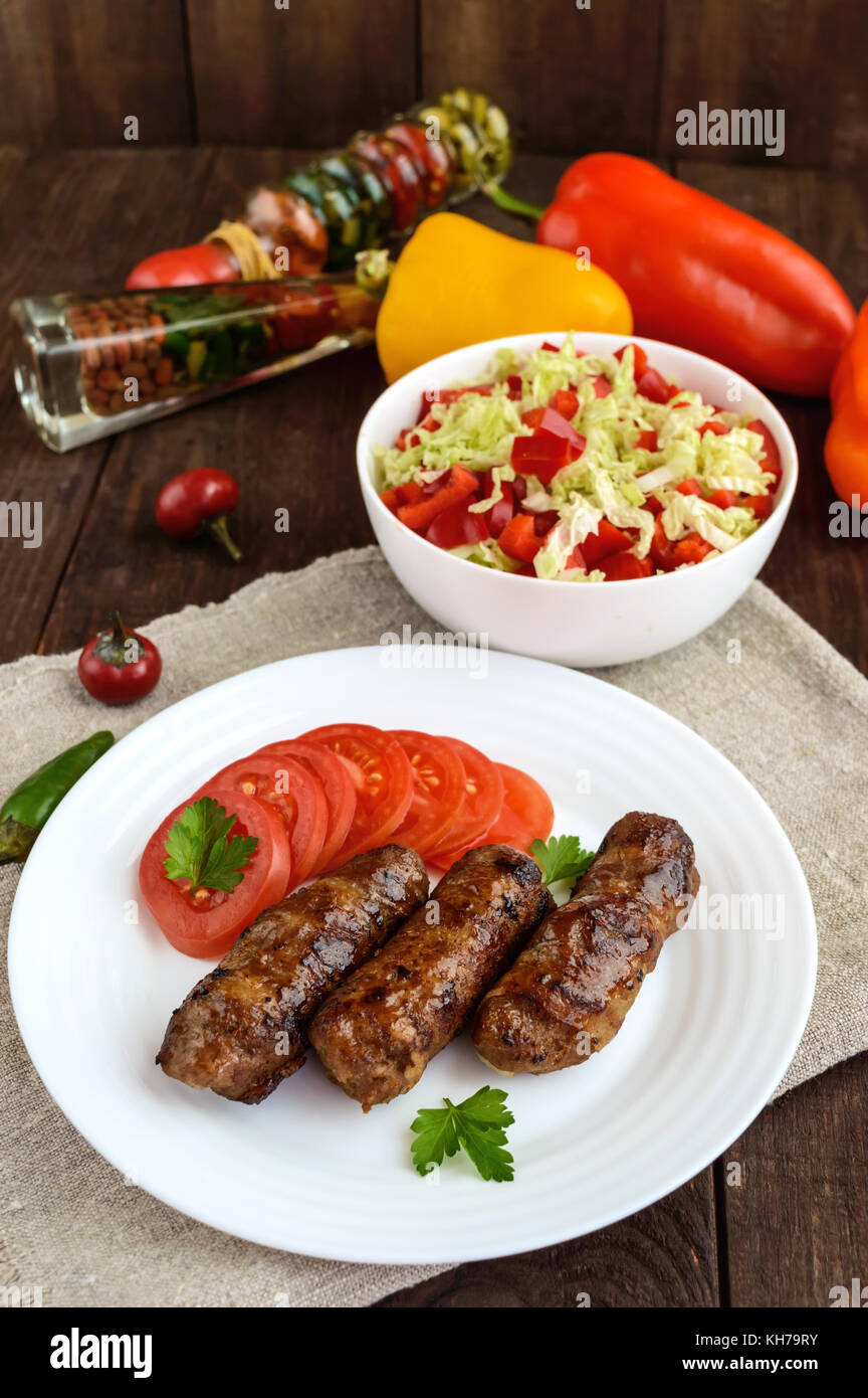Juicy grilled rolls of minced meat wrapped in bacon with fresh tomato ...