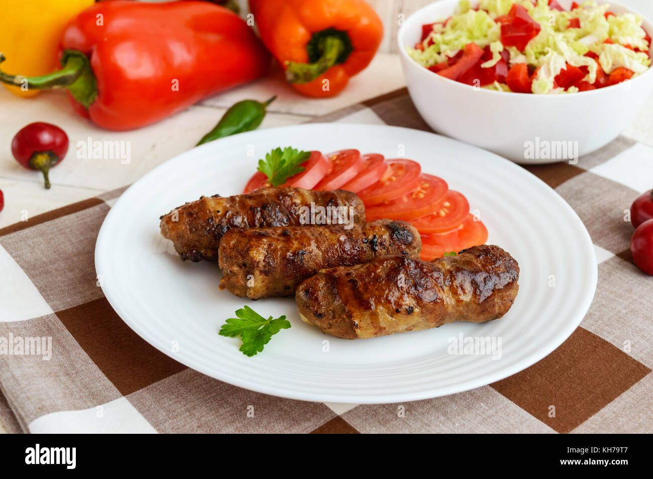 Juicy grilled rolls of minced meat wrapped in bacon with fresh tomato ...