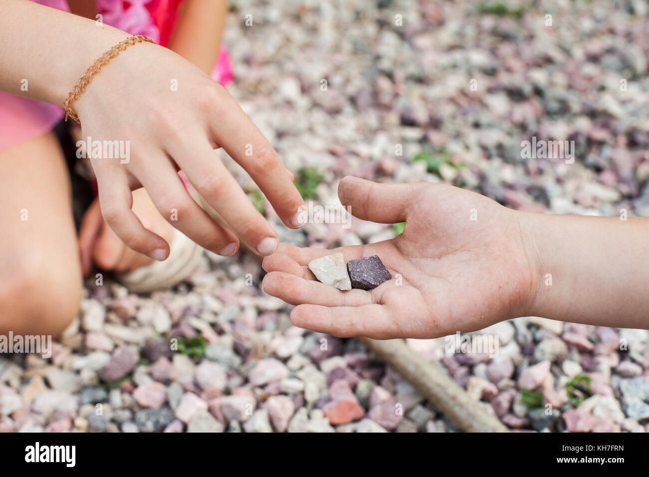 Little girl taking stones from friends hand Stock Photo - Alamy