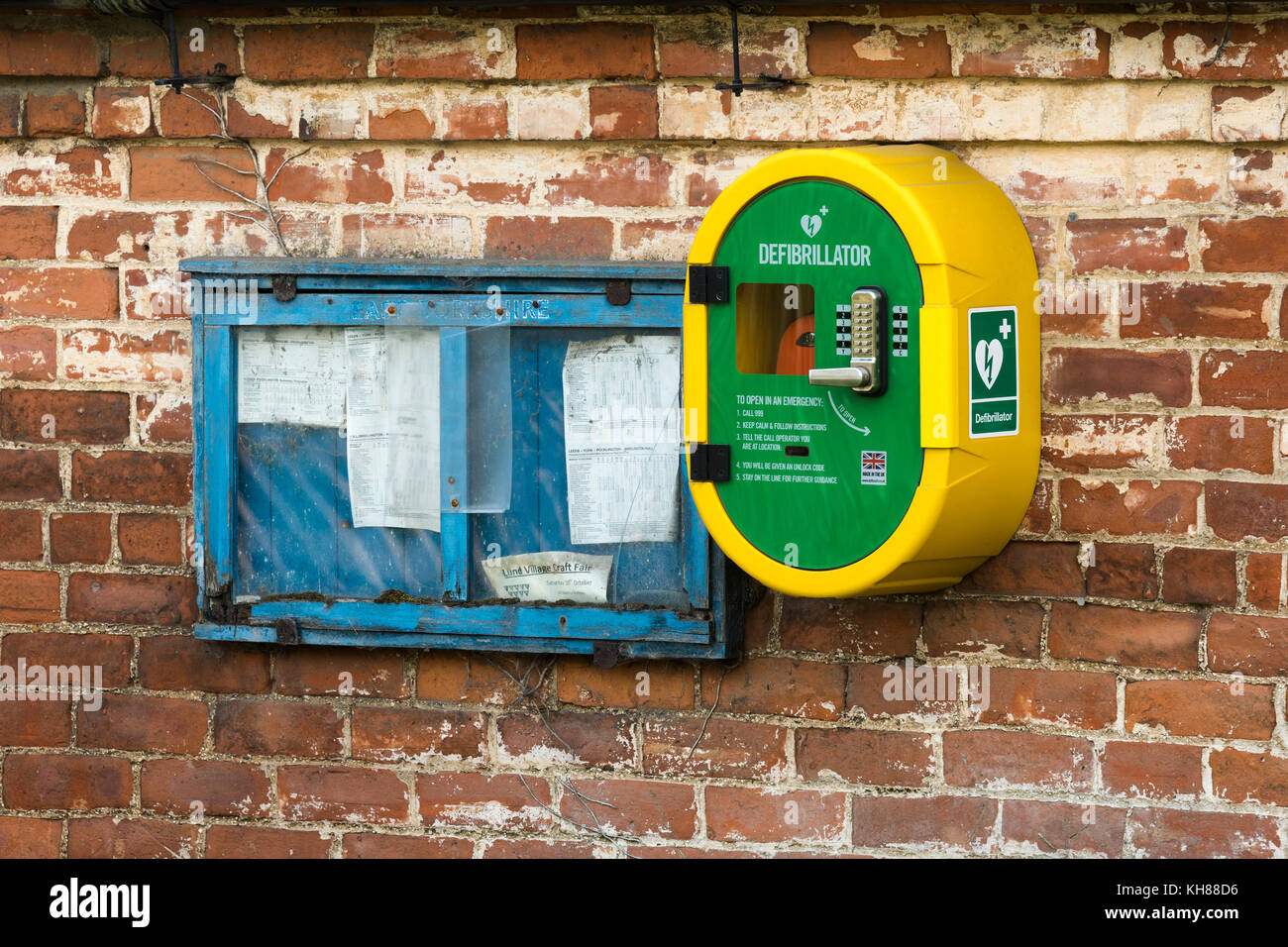 Emergency life saving defibrillator & old village notice board side by ...