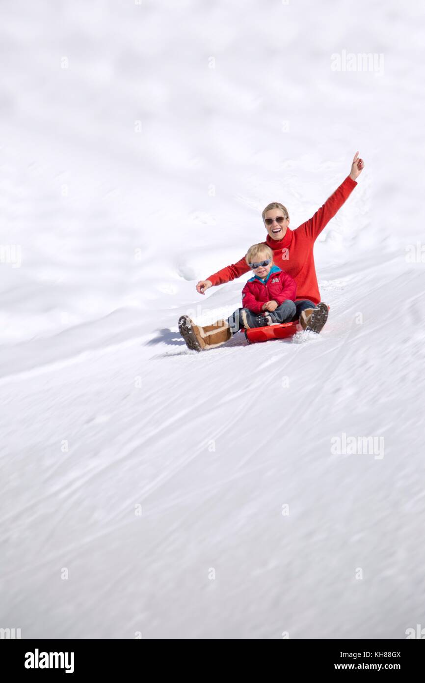 Portrait of smiling woman sitting with her childs on sled in snow ...